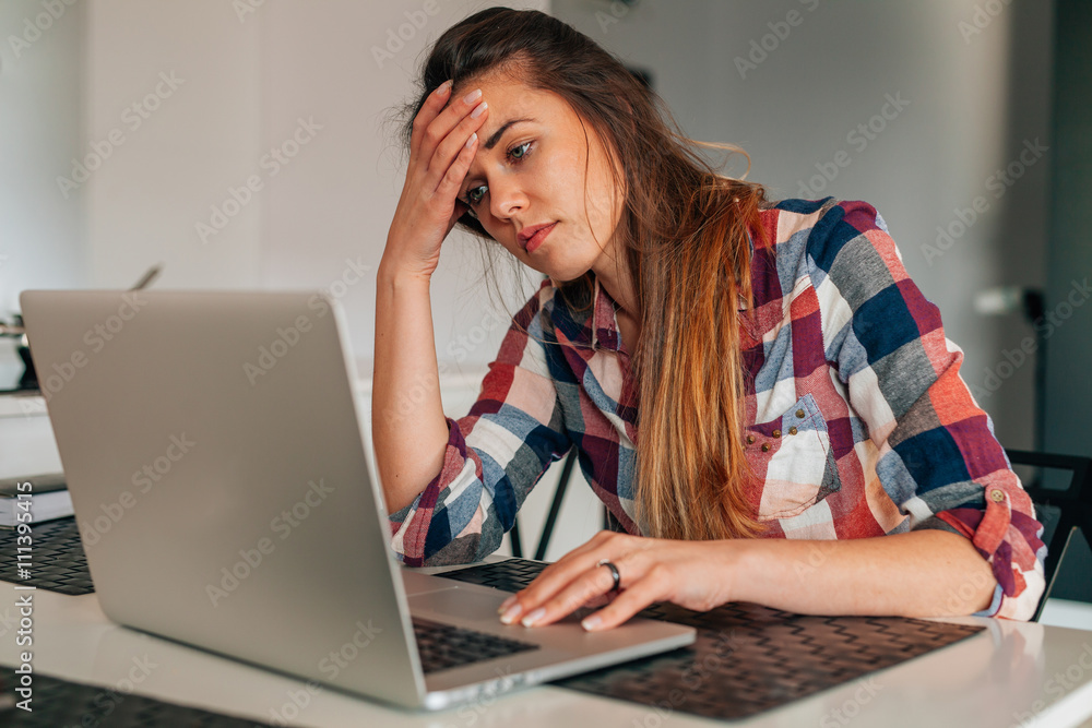 Sad girl sitting i the kitchen and using laptop. Stock Photo | Adobe Stock