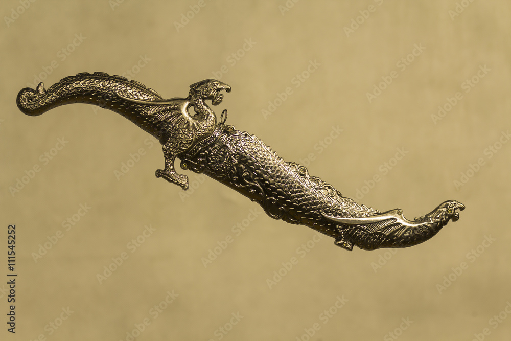 decorative carved dagger with heads of dragons in a sheath on a gray ...
