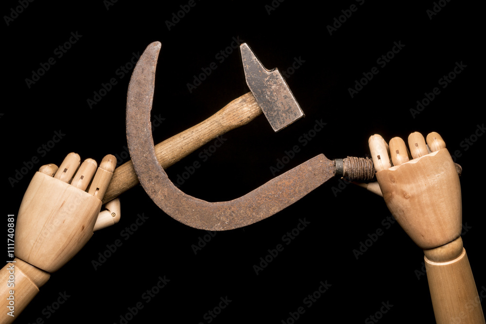 Two wooden hands brandishing a rusty sickle and a used hammer. On black ...