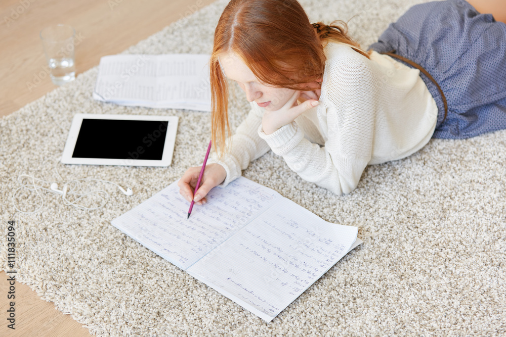 Pretty young Caucasian woman lying on the floor and making notes in ...