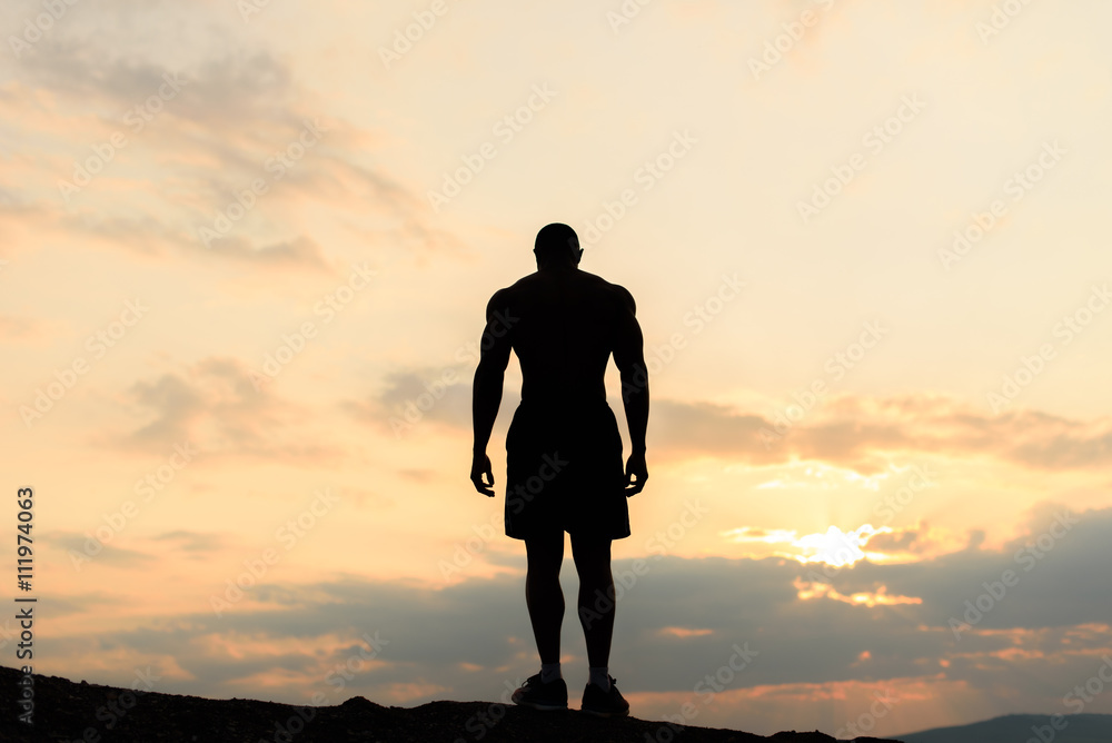 Back view on silhouette of bodybuilder posing at the sunrise or sunset ...