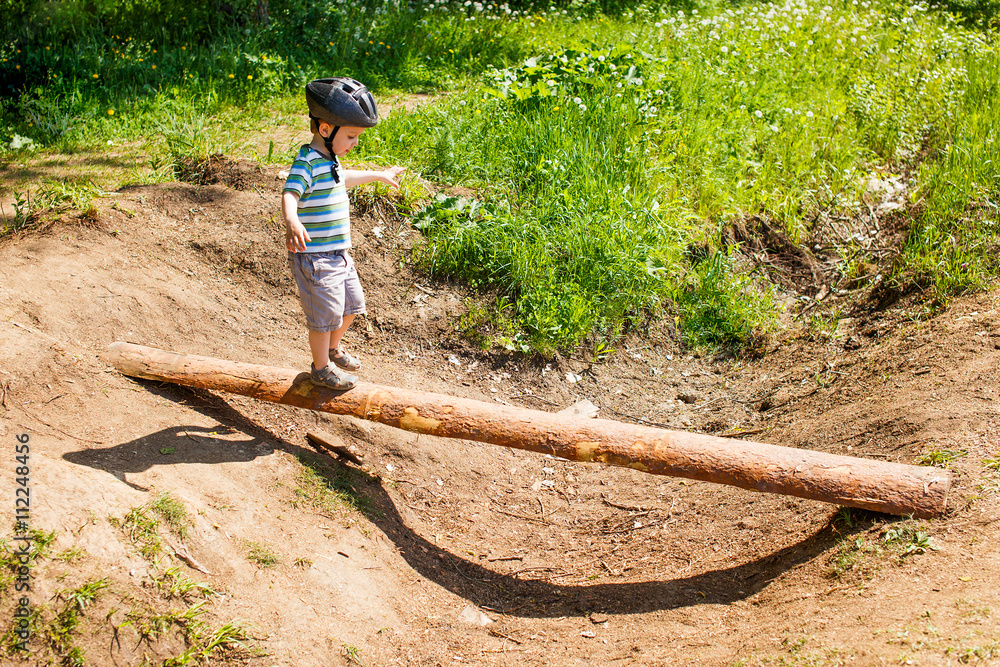 little boy in a sports helmet goes on a log. child is balancing on a ...