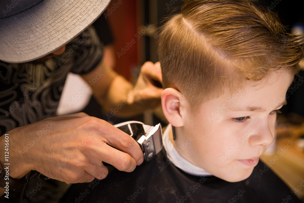 Close-up of man hands grooming kid boy hair in barber shop. Boy cut ...