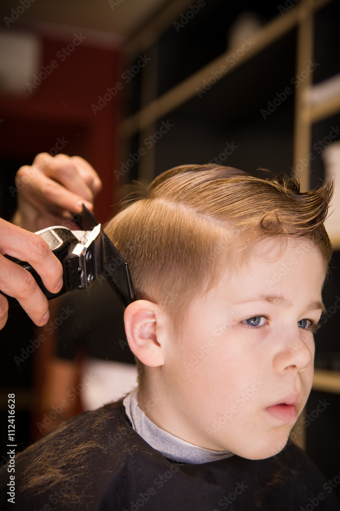 Close-up of man hands grooming kid boy hair in barber shop. Boy cut ...