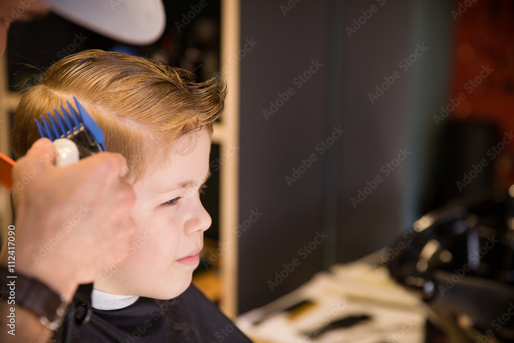 Close-up of man hands grooming kid boy hair in barber shop. Boy cut ...