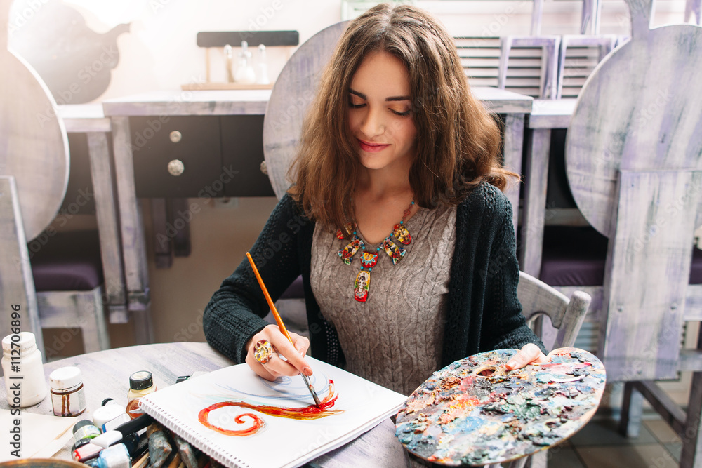 Pretty smiling young woman drawing a picture with poster paint. Front ...
