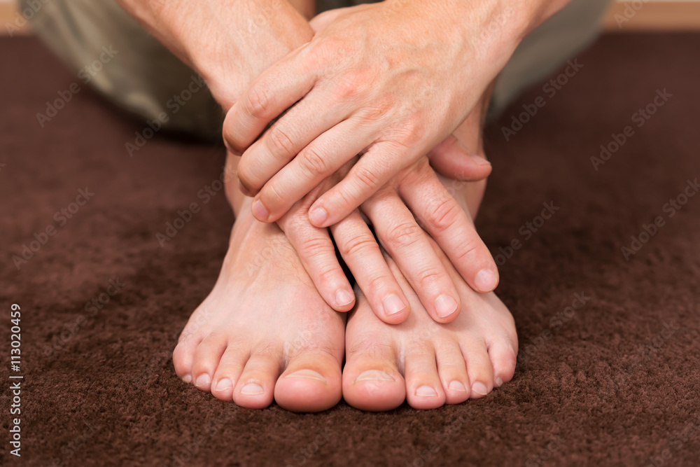 Male hands crossed over healthy resting feet. Stock Photo | Adobe Stock