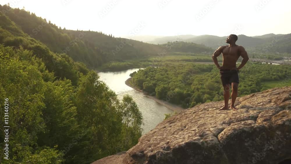 African american man body builder stands on a rock against the blue ...
