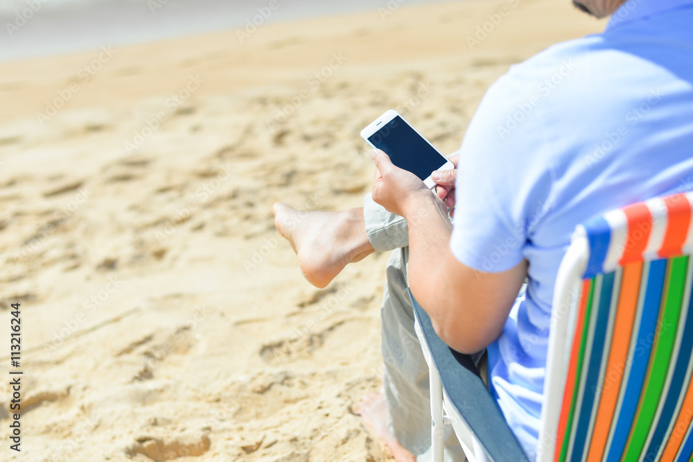 Closeup on man chilling on the beach using smartphone. Back side view ...