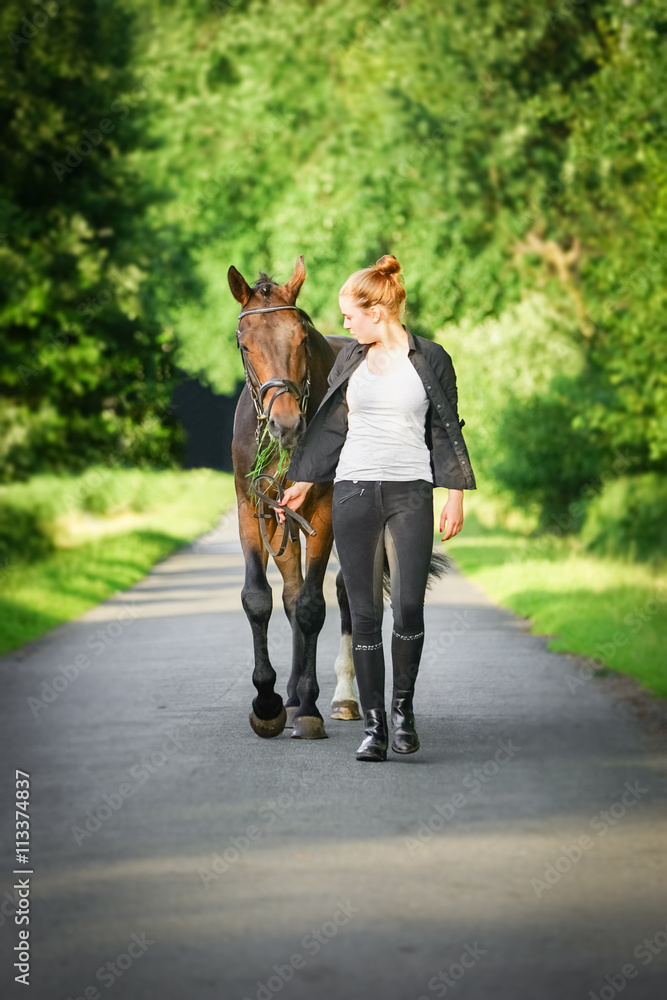 Junge, hübsche Reiterin führt Pferd am Halfter einen Weg entlang Stock ...