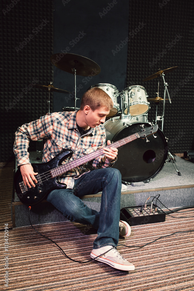 Bass guitar player sitting near drum set at music studio. Musician ...