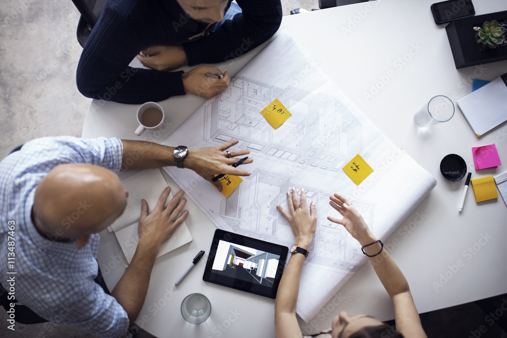Overhead view of architects discussing over blueprints and digital ...