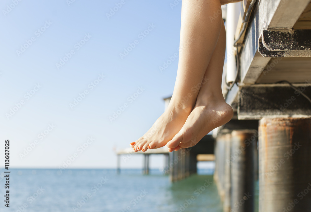 Woman's feet dangle from jetty foto de Stock | Adobe Stock