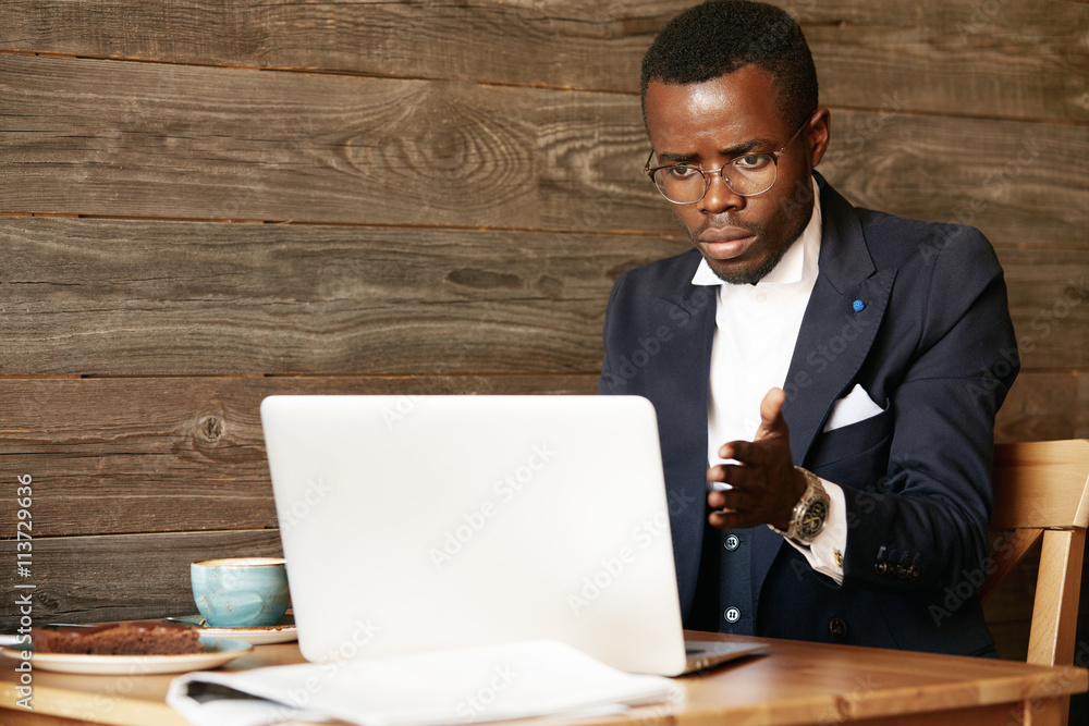 Worried young African businessman, sitting in front of laptop, looking ...