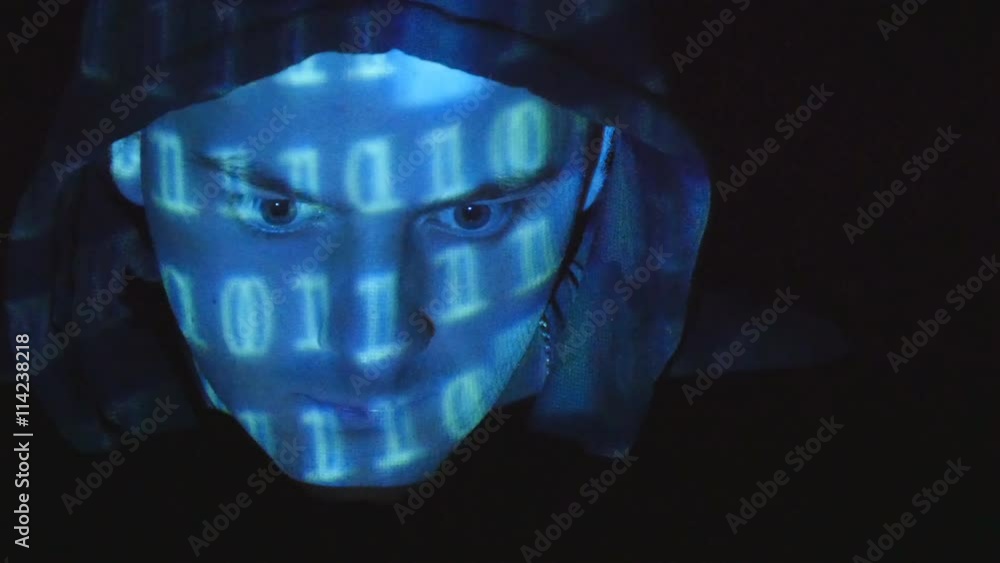 Close up shot of male face of hacker with binary code projections. Source code projected over an ...