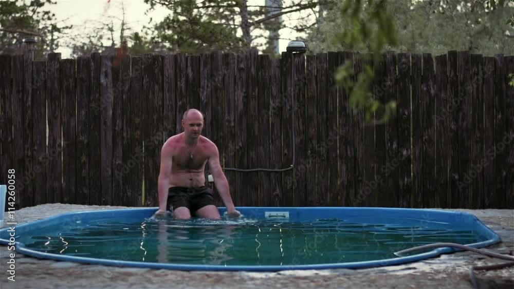 A young boy touches the feet of the cold water in the pool. Slow motion ...