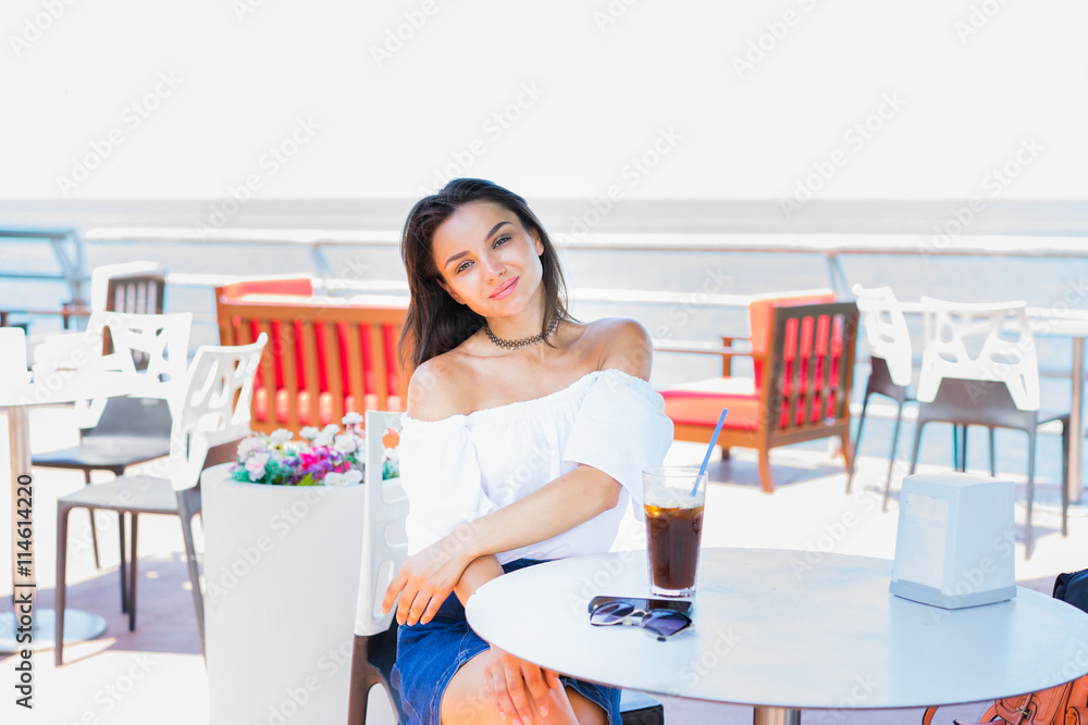 Woman sitting in cafe with ice coffee with sky and sea background ...