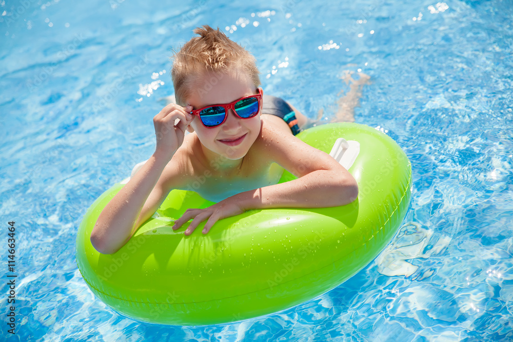 Little boy swimming in the pool with big bright green rubber ring ...