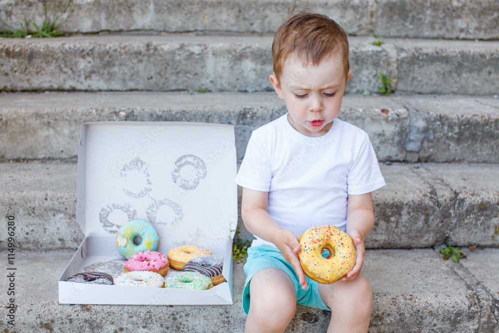 child sitting on the steps with a box of donuts. little boy playing ...