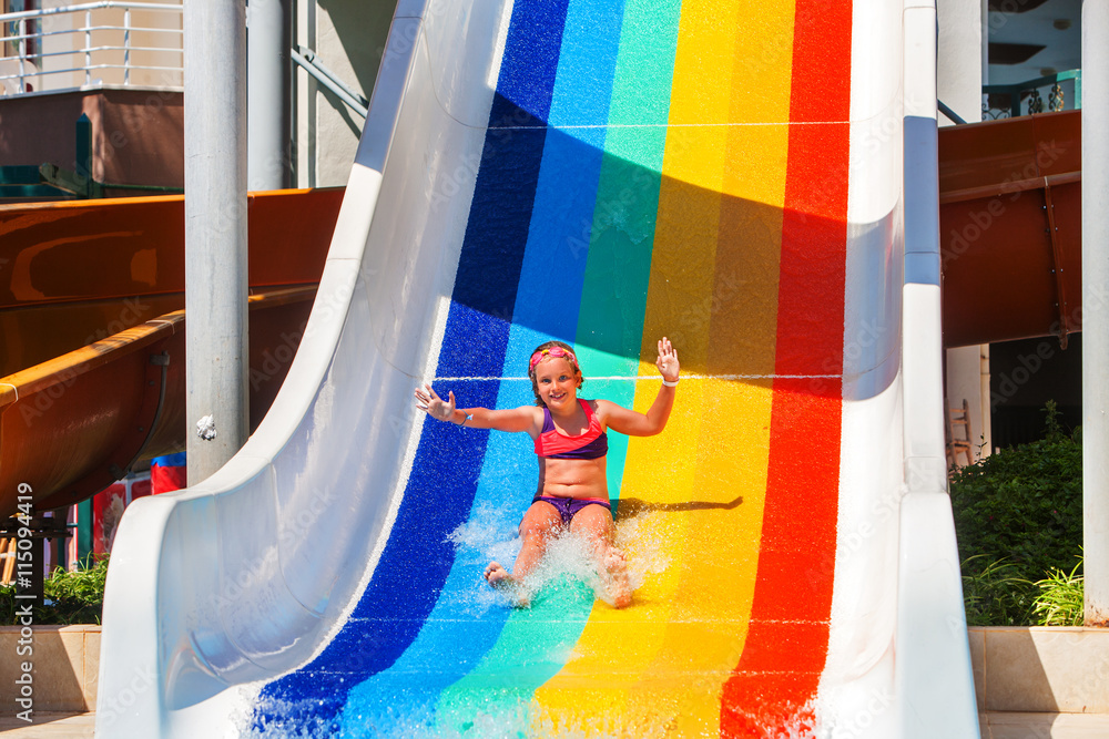 Child little girl on water slide at aquapark show hands up. There are ...