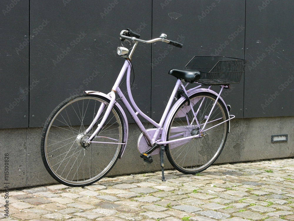 Hollandrad oder Damenrad in Lila mit Fahrradkorb auf Kopfsteinpflaster im Sonnenschein im ...