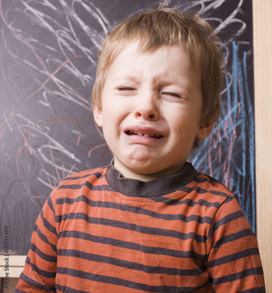 little cute real boy screaming and crying at school near blackboard ...