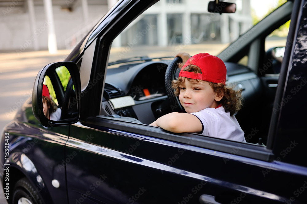 child with curly hair and a red cap sits behind the wheel of a car ...