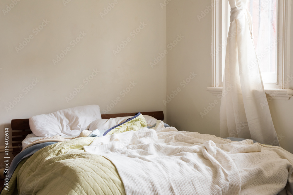 Unmade futon style bed with wooden bedhead with rumpled sheets, pillows ...