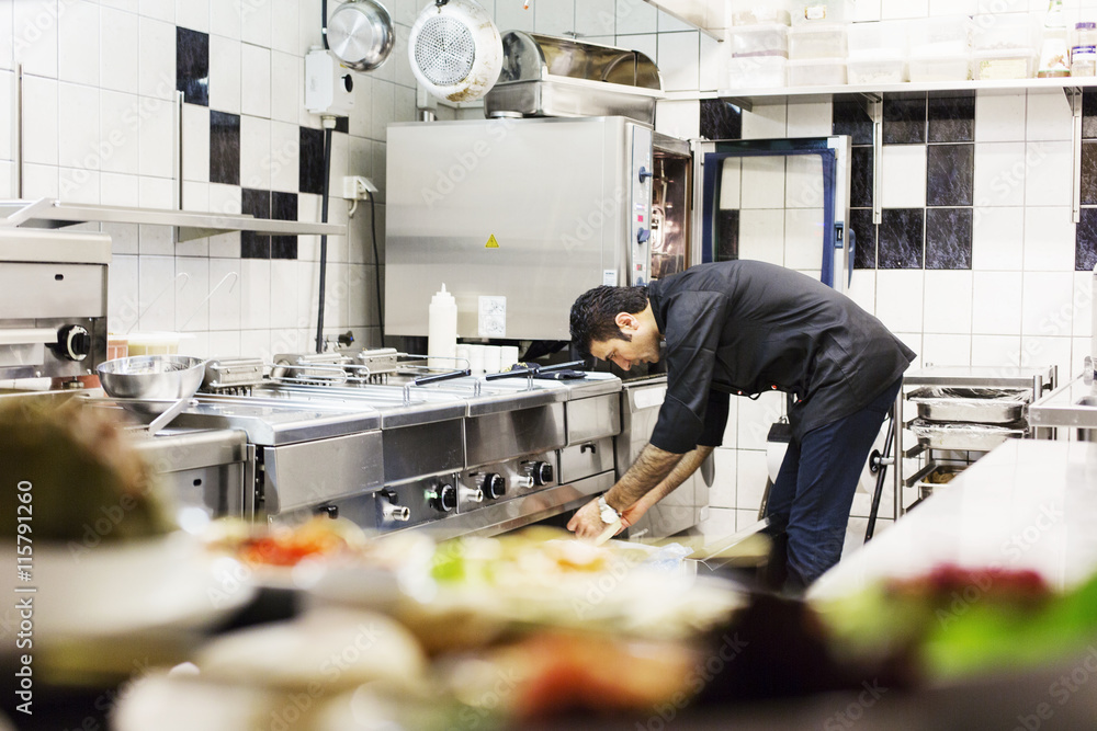 Side view of male chef working in commercial kitchen at Lebanese ...