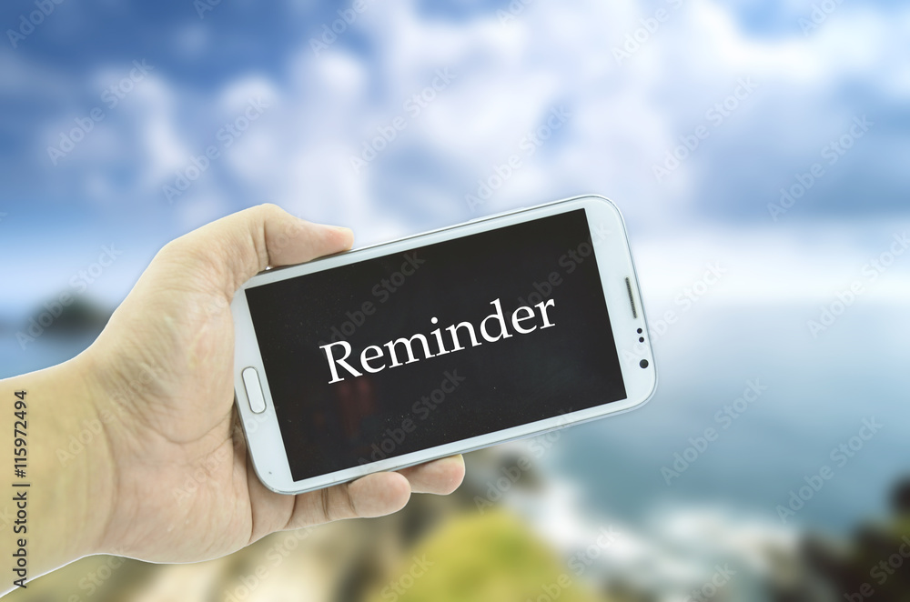 Conceptual image cropped hand holding mobile phone with word reminder ...