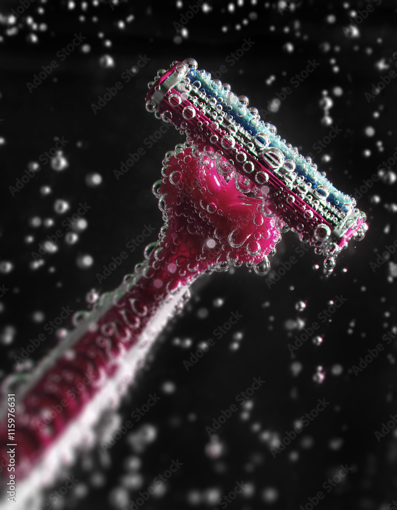 Pink razor blade close up in cold water with bubbles on black ...