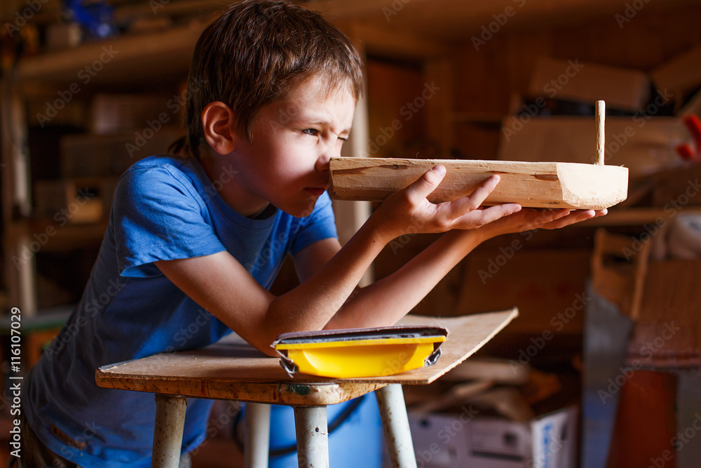 boy builds a toy ship of wood. child in the workshop makes crafts. toy ...