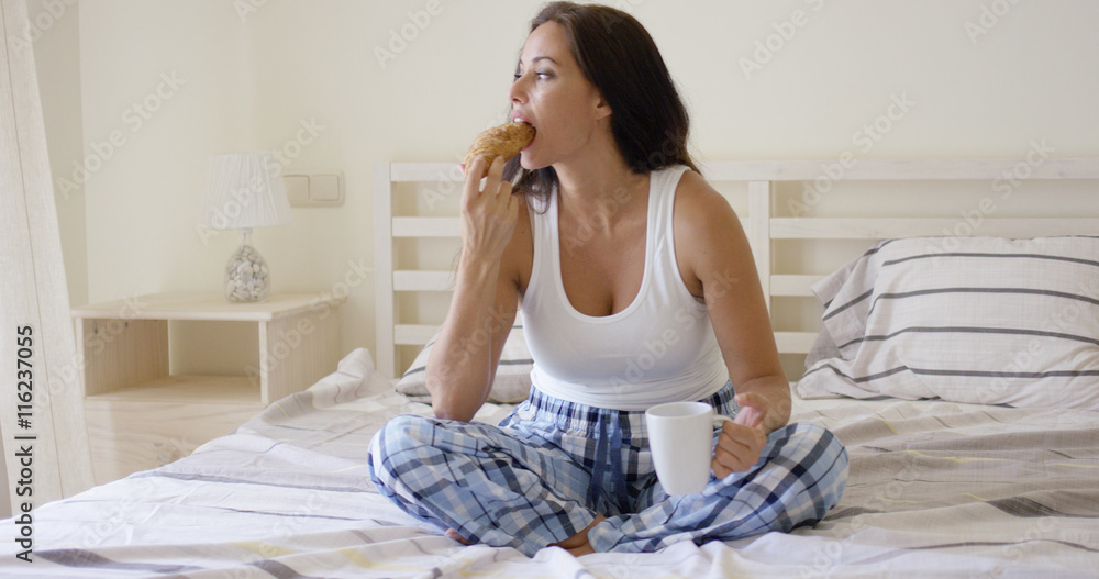 Attractive young woman having her breakfast as she sits cross-legged on ...