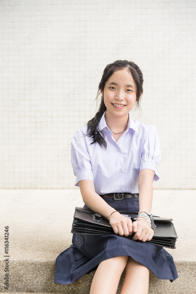 Cute Asian Thai high schoolgirl student in school uniform sitting on the stair and showing ...