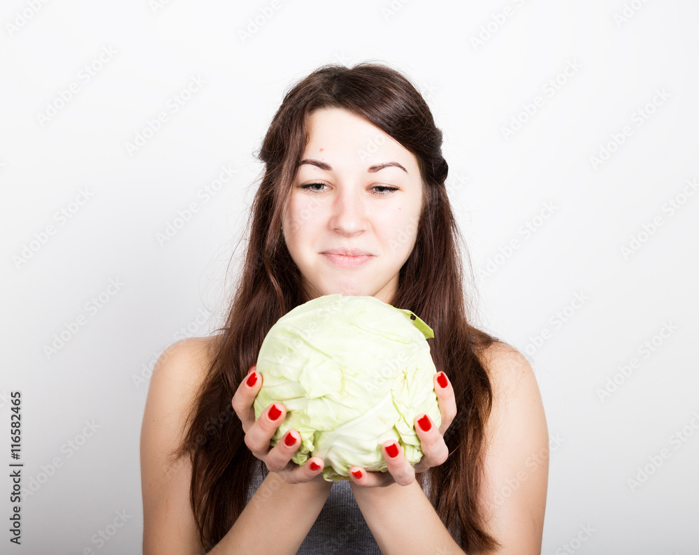 beautiful young woman eating an vegetables. holding cabbage, she stares ...