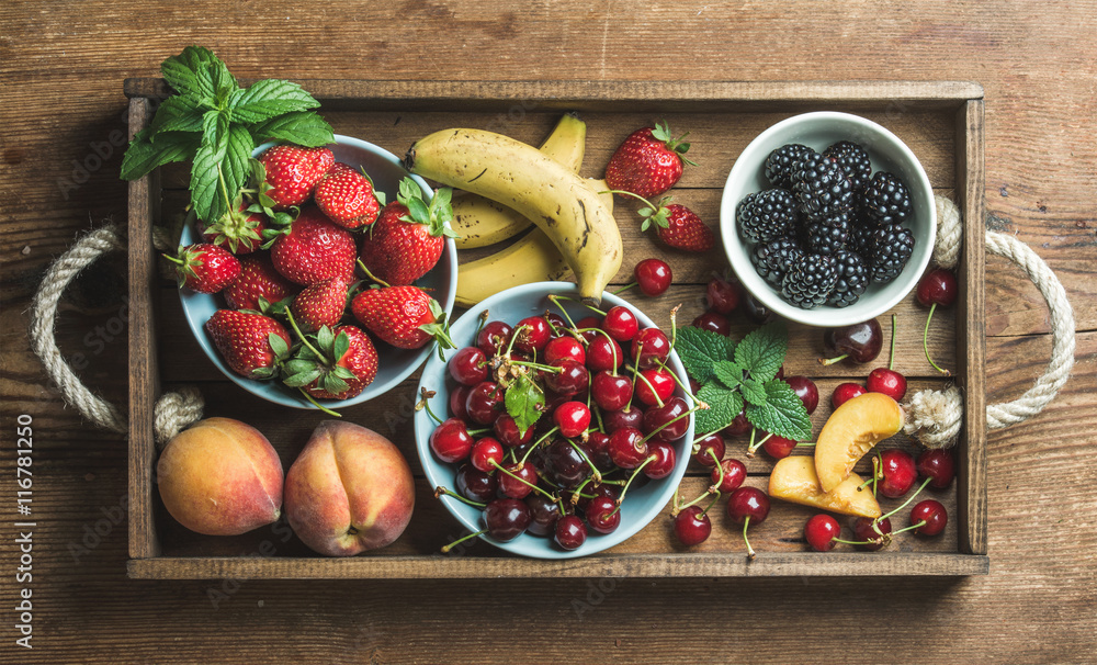 Summer fresh fruit and berry variety in rustic wooden tray over wooden ...
