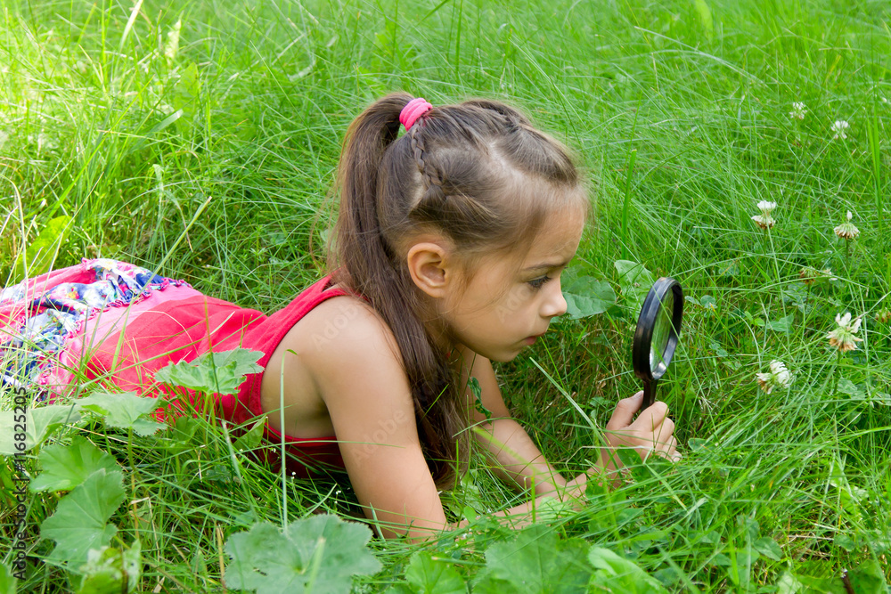 Young girl exploring nature in a meadow looking at magnifying glass ...