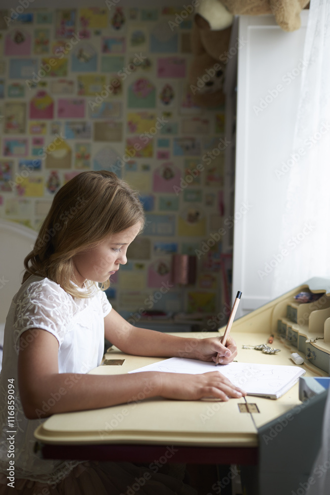 Girl writing in notebook while sitting at desk Stock Photo | Adobe Stock