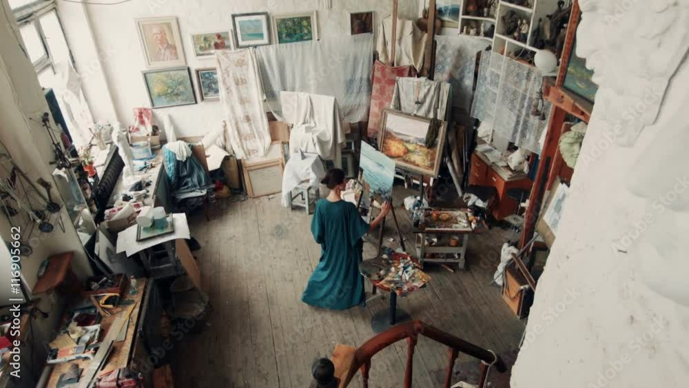 Wide view of a female artist wearing a smock standing in her studio ...