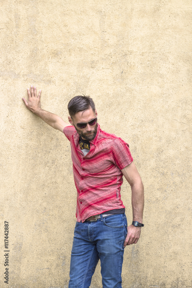 Tough guy posing with one hand resting on a wall and the other hand in ...