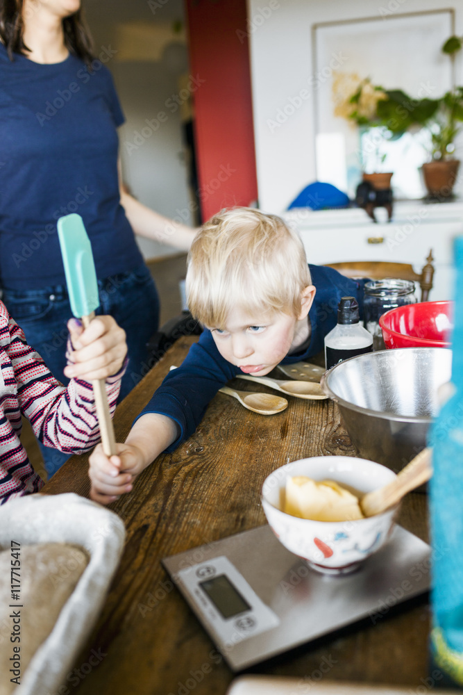 Little boy with sister holding scraper while mother standing at table ...