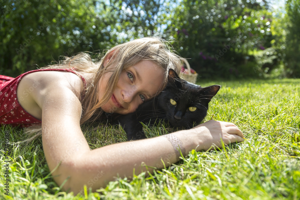 Smiling little girl lying on meadow with black cat Stock Photo | Adobe ...