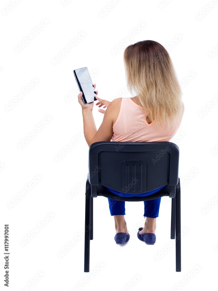 back view of woman sitting on chair and looks at the screen of the ...