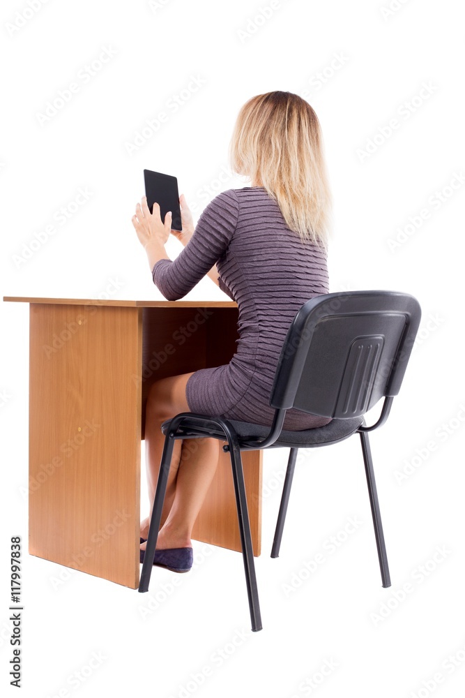 back view of woman sits by the table and looks at the screen of the ...