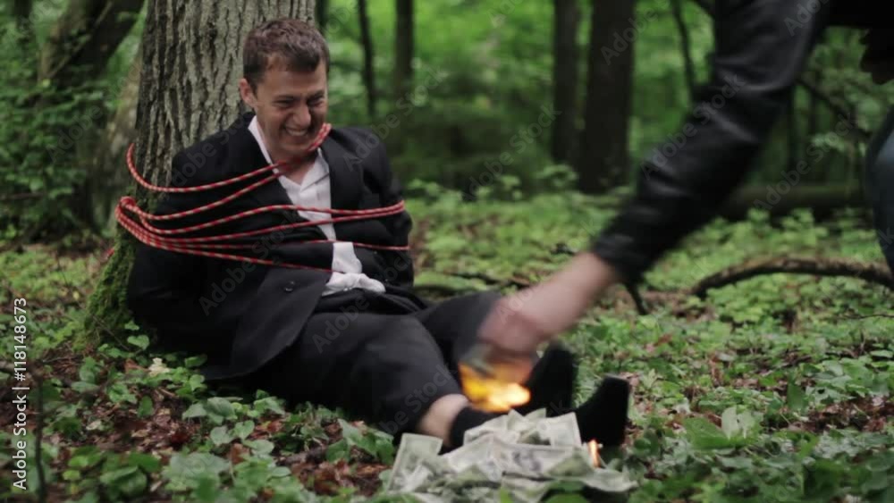 Businessman tied to a tree frantically tries to to put out burning ...