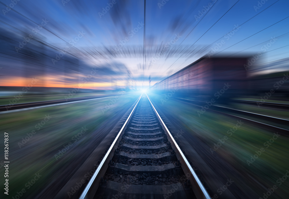 Railway station with cargo wagons and train light in motion at sunset ...