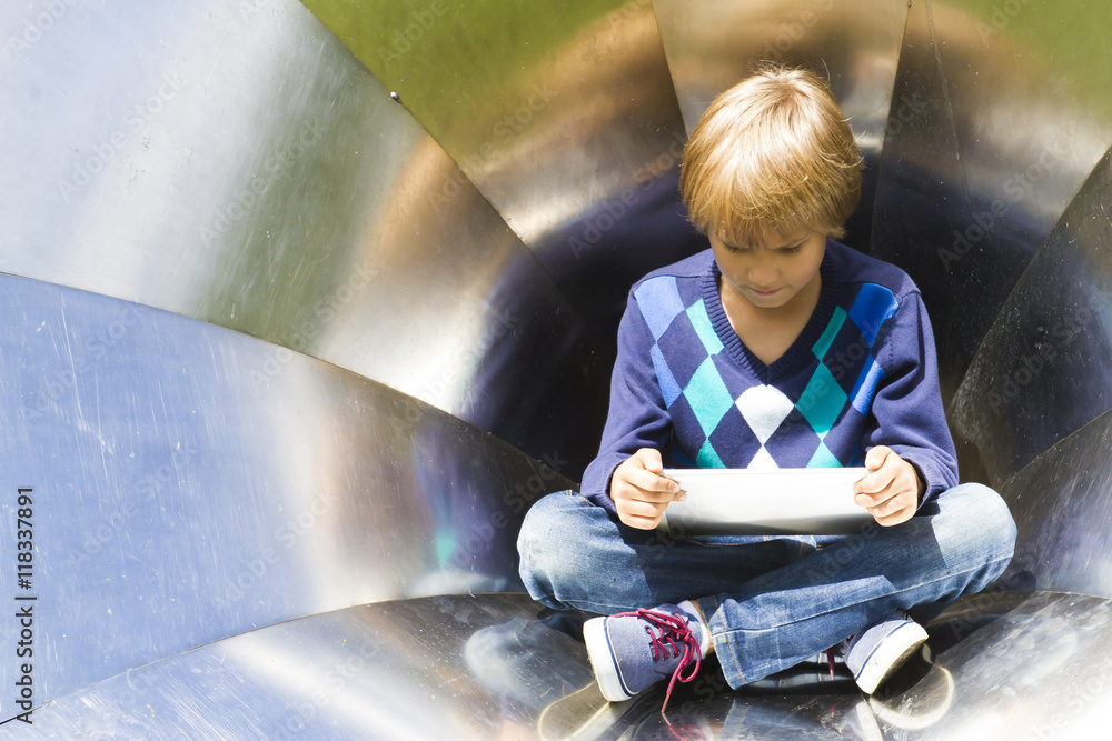 Little boy with tablet PC outdoor. Child looking down to the screen ...