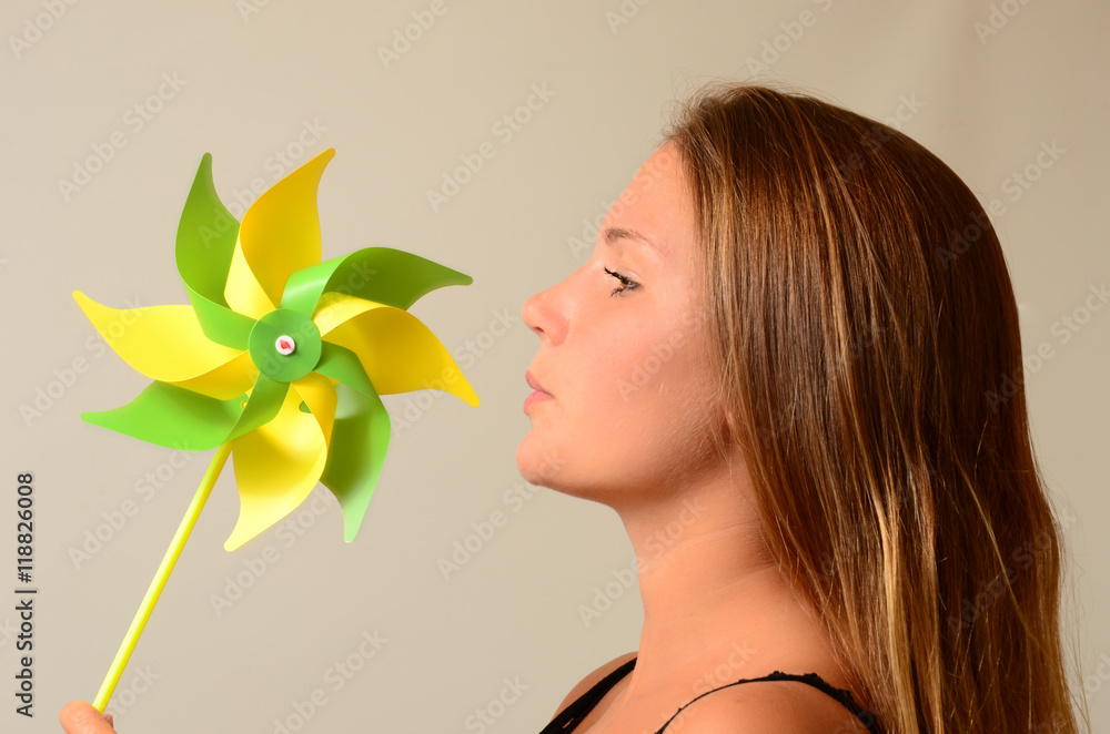junge Frau pustet in gelb-grünes Windrad Stock Photo | Adobe Stock