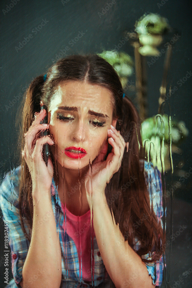 Girl talking on phone and crying. Girl is crying behind window with ...