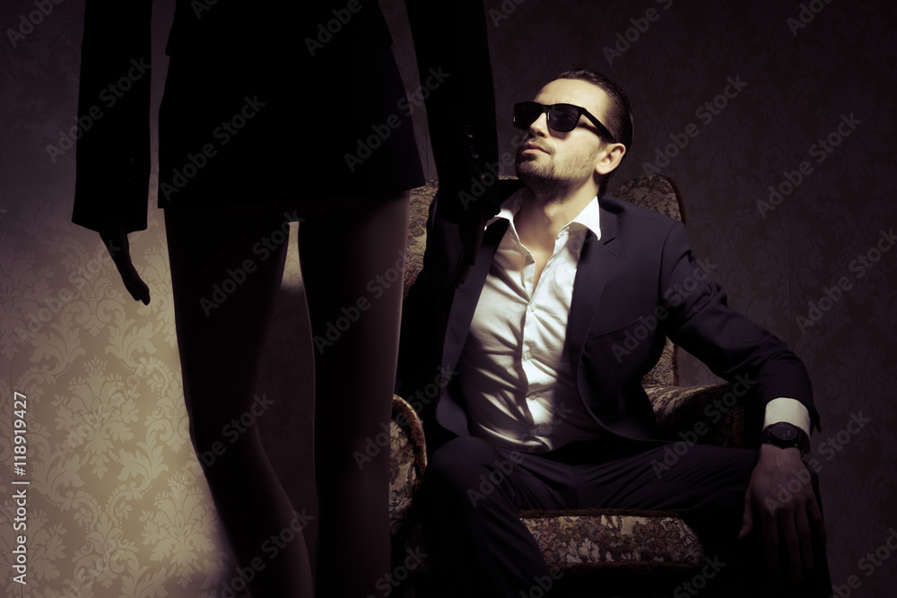 Young and elegant man sitting in chair looking at woman standing in ...